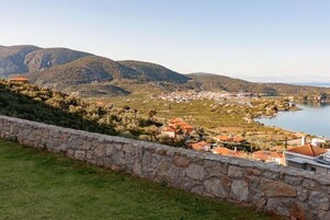 Uma vila costeira com muros de pedra, vinhedos em terraços e um corpo d'água.