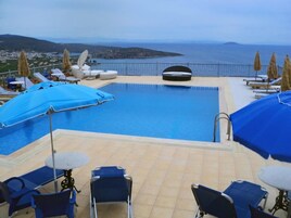 Piscina no terraço com espreguiçadeiras e guarda-sóis, com vista para um corpo de água e terra distante.