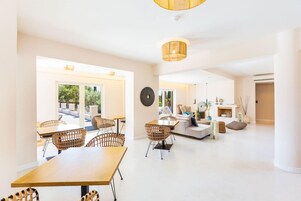 Um espaço amplo e interno com mesa de jantar, cadeiras, um sofá e um lustre.