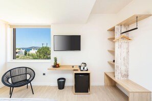Quarto moderno com uma janela ampla, televis ão de tela plana, pequena área de cozinha com cafeteira e uma cadeira preta.
