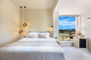 Quarto moderno com uma cama grande, vista para o exterior e uma pequena cozinha.