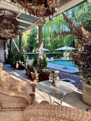 Área de pátio ao ar livre com móveis de vime, plantas em vasos e vista para uma piscina.