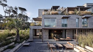 Um edifício moderno de vários andares com telhado plano, área de estar ao ar livre e um jardim com diversas plantas.