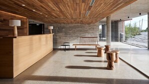 Uma área de recepção moderna com balcão de madeira, um banco e banquetas de madeira.