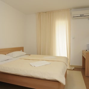 Quarto de hotel com cama, mesa de cabeceira, aparelho de ar condicionado e janela com cortinas.