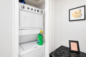 Uma lavanderia com máquina de lavar, um frasco de detergente e um quadro em cima do balcão.