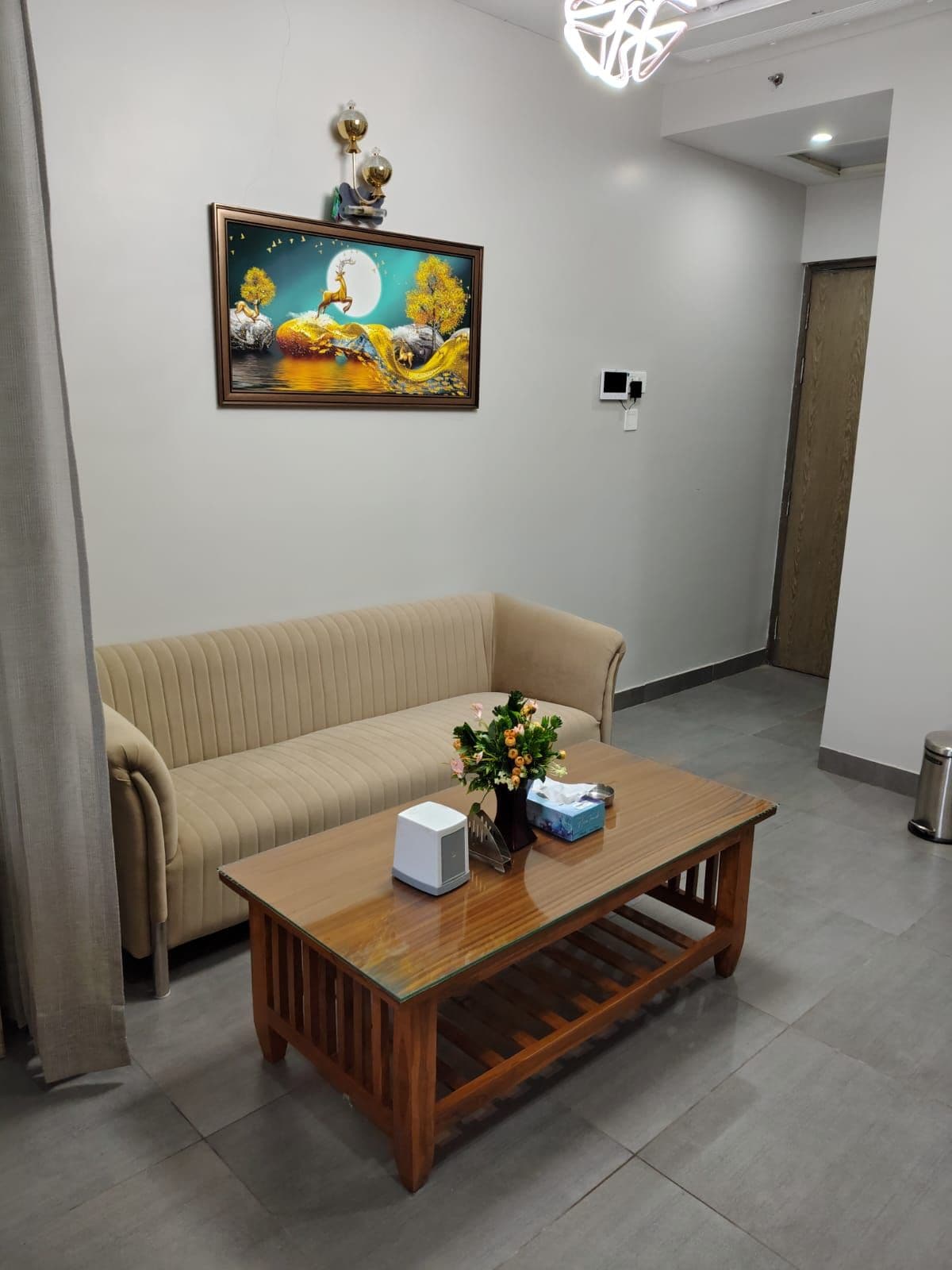 Uma sala de estar moderna com um sofá bege, uma mesa de centro de madeira e uma pintura de uma paisagem com um veado.
