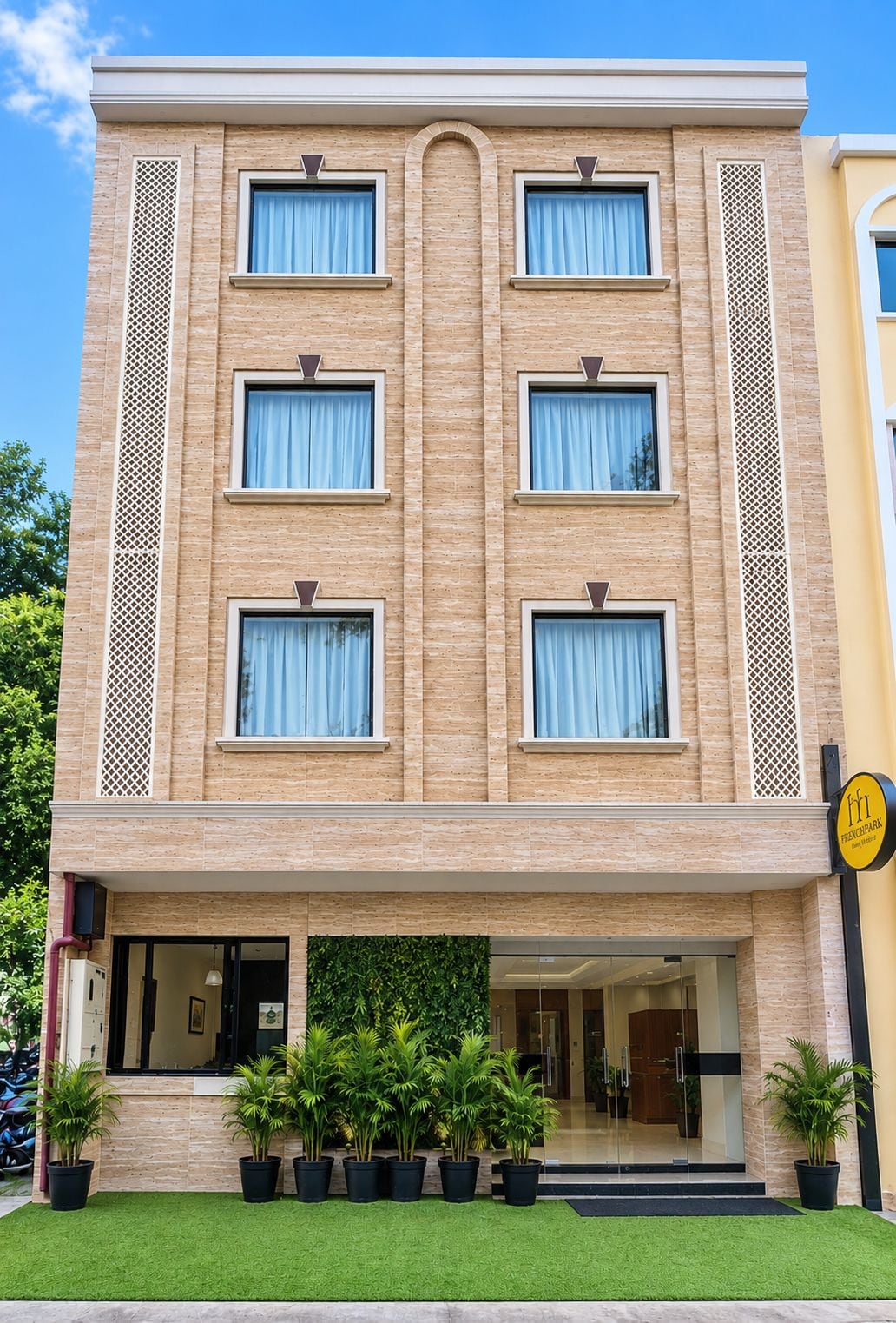 Um hotel de vários andares com fachada de tijolos, grandes janelas com cortinas e entrada bem cuidada com plantas em vasos.