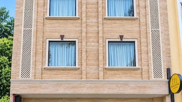 Um hotel de vários andares com fachada de tijolos, grandes janelas com cortinas e entrada bem cuidada com plantas em vasos.