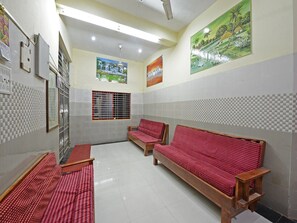 Quarto com piso de azulejos, duas bancos de madeira com almofadas vermelhas, janela com grades de metal e tomadas fixadas na parede.