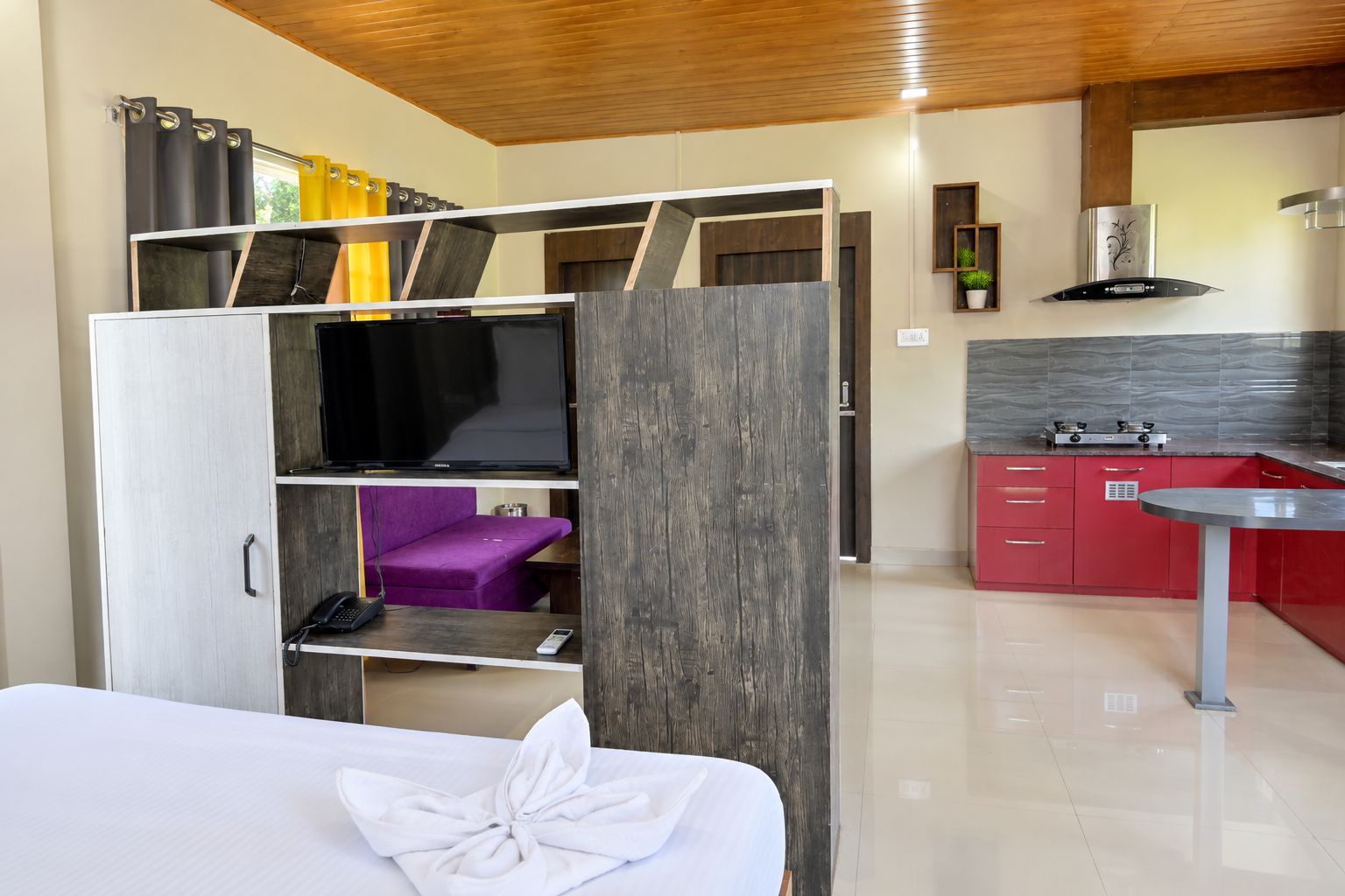 Quarto de hotel moderno com cama, televisão, cozinha compacta e banheiro.