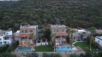Área residencial com dois edifícios de pedra, piscina e paisagem verde exuberante.