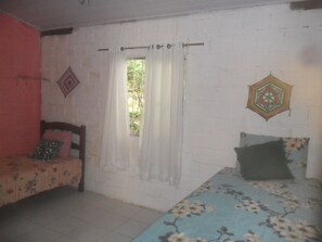 Quarto com duas camas, uma janela com cortinas e uma parede com decoração geométrica.