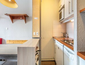 Cozinha compacta com micro-ondas, fogão e pia. Possui um banco de madeira e uma pequena prateleira.