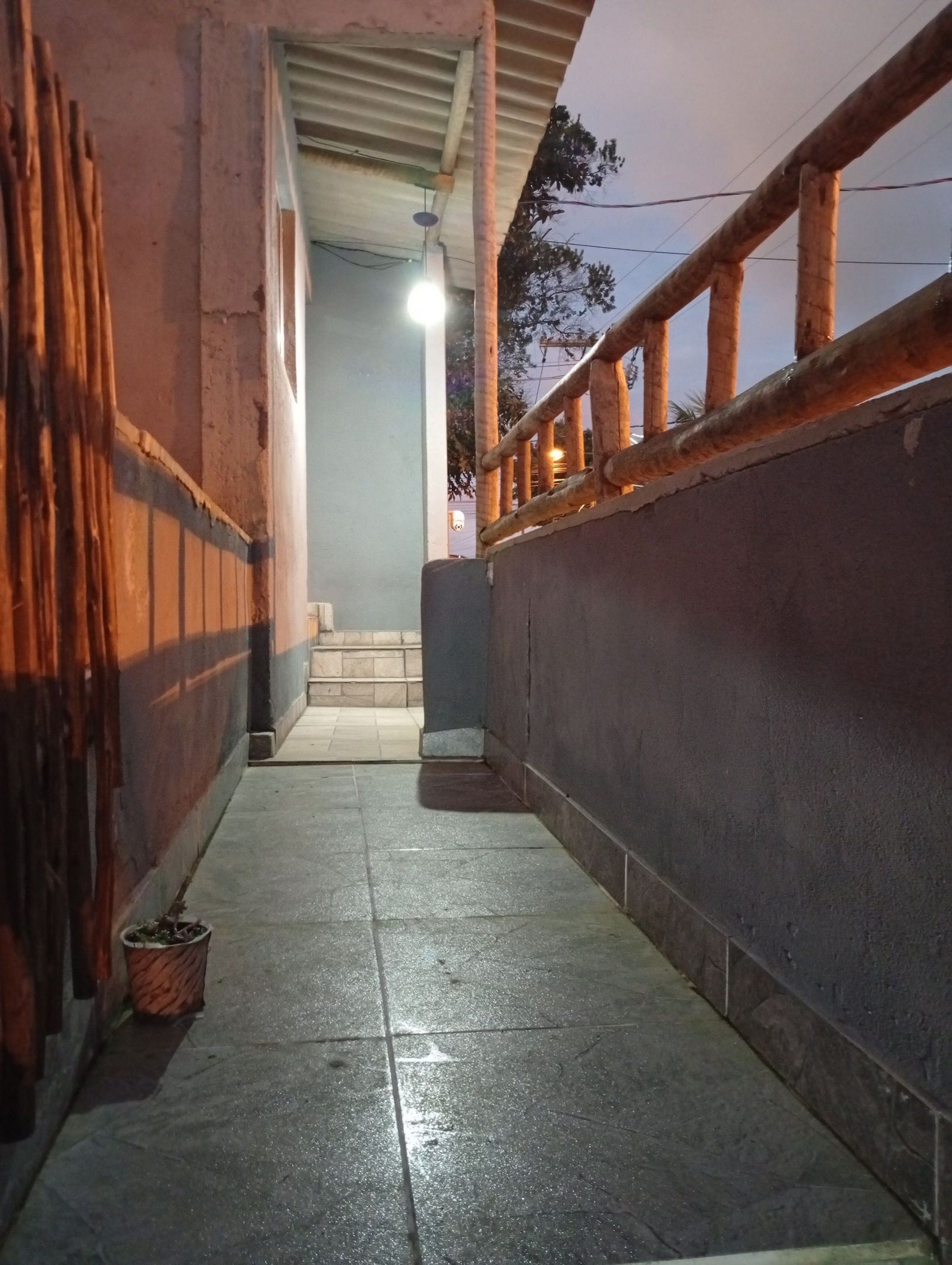 Um corredor estreito com piso ladrilhado, guarda-corpo de madeira de um lado e parede de concreto do outro.
