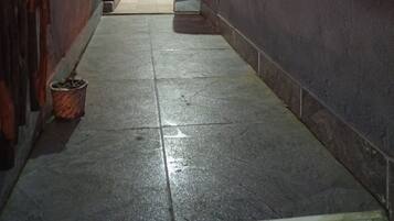 Um corredor estreito com piso ladrilhado, guarda-corpo de madeira de um lado e parede de concreto do outro.