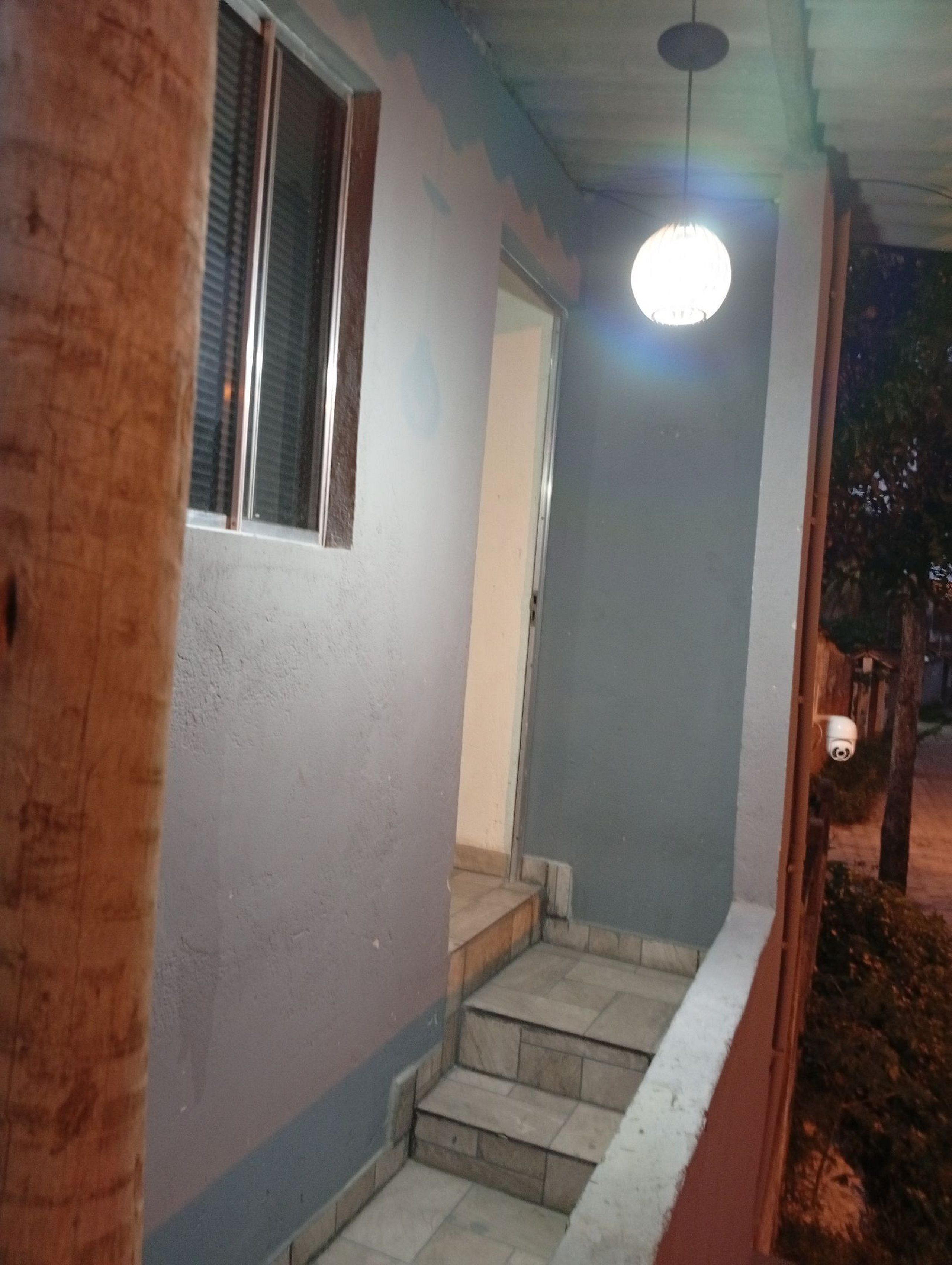Escada que leva a uma porta com câmera de segurança, janela com persianas e luminária acima.