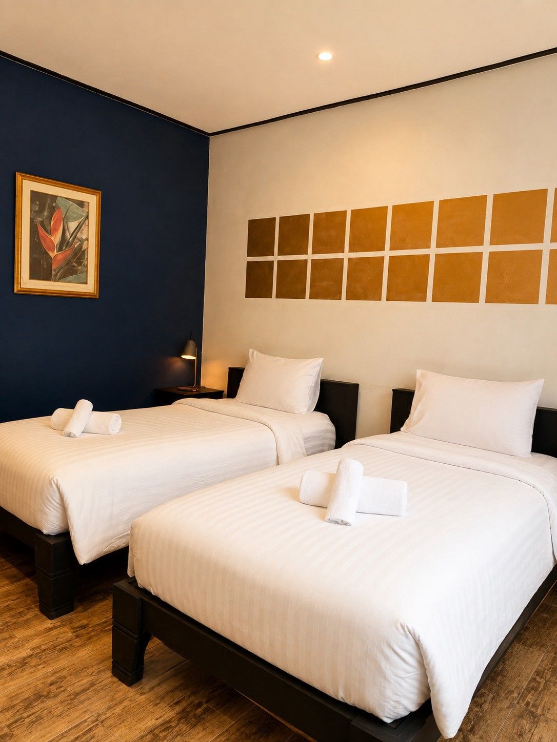 Quarto de hotel com duas camas, mesa de cabeceira, abajur e quadro na parede.