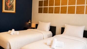 Quarto de hotel com duas camas, mesa de cabeceira, abajur e quadro na parede.