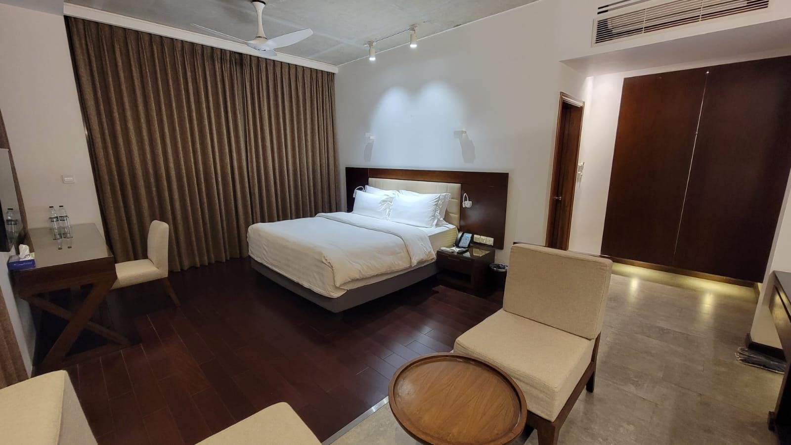 Quarto de hotel com cama, escrivaninha com cadeira, mesa redonda e guarda-roupa.