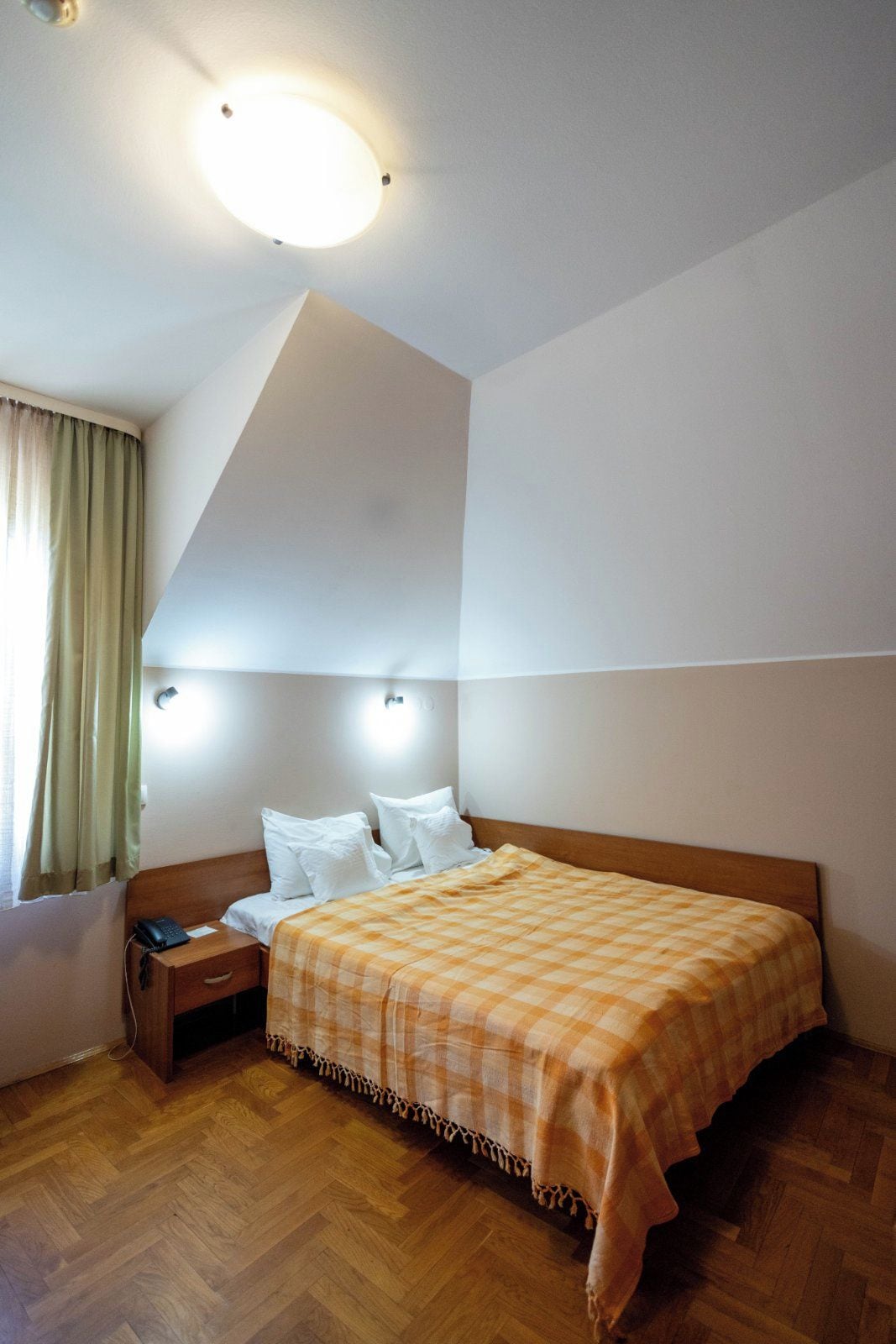 Quarto de hotel com cama, mesa de cabeceira, telefone e luminária no teto.