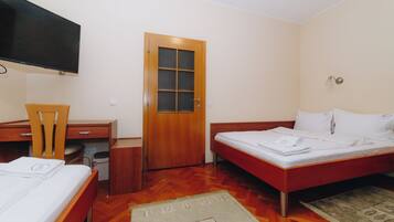 Quarto de hotel com cama, escrivaninha, cadeira, televisão e porta.