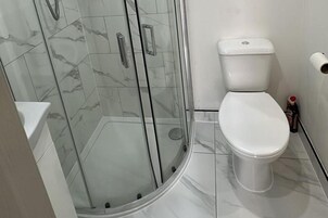 Casa de banho com cabine de chuveiro em vidro, sanita branca e lavatório branco.