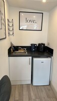 Uma cozinha compacta equipada com pia, chaleira, cafeteira e geladeira.