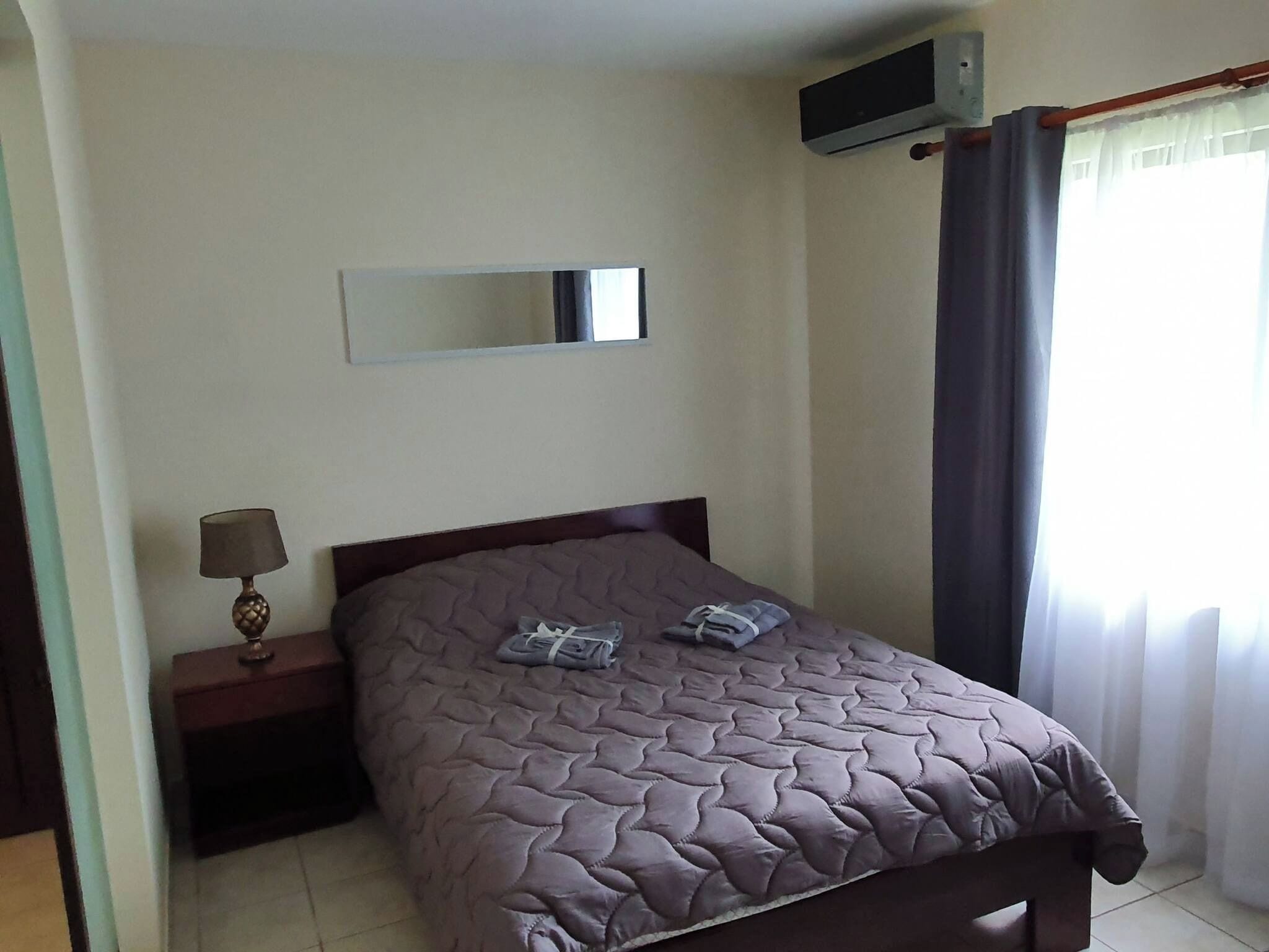 Quarto com cama, mesa de cabeceira, luminária, espelho e aparelho de ar condicionado.