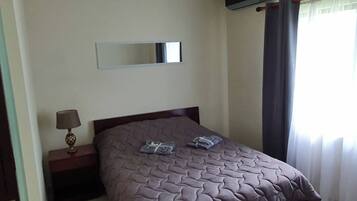 Quarto com cama, mesa de cabeceira, luminária, espelho e aparelho de ar condicionado.