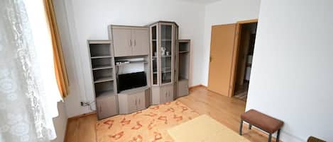 Quarto com piso de madeira, armário com portas de vidro, um banco e porta que dá para outro cômodo.