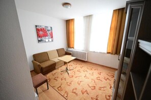 Quarto com sofá, uma pequena mesa, radiador e janela com cortinas.