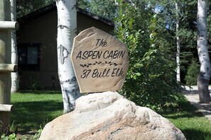 Uma placa de madeira com o texto 'The Aspen Cabin 37 Bull Elk' sobre uma rocha.