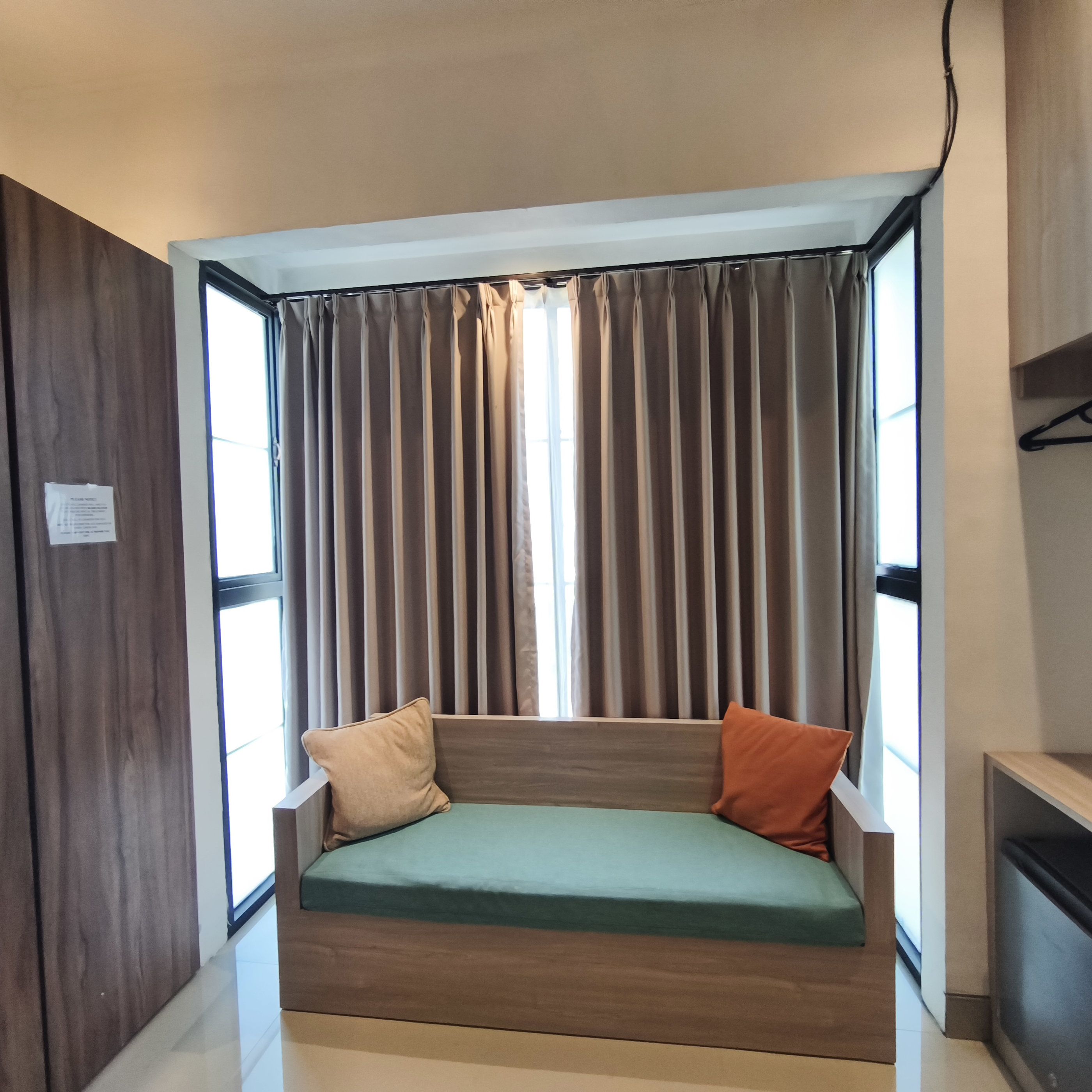 Quarto de canto com sofá embutido, janelas amplas com cortinas e parede de madeira.