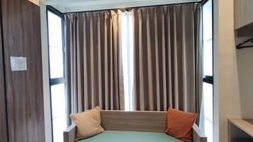 Quarto de canto com sofá embutido, janelas amplas com cortinas e parede de madeira.