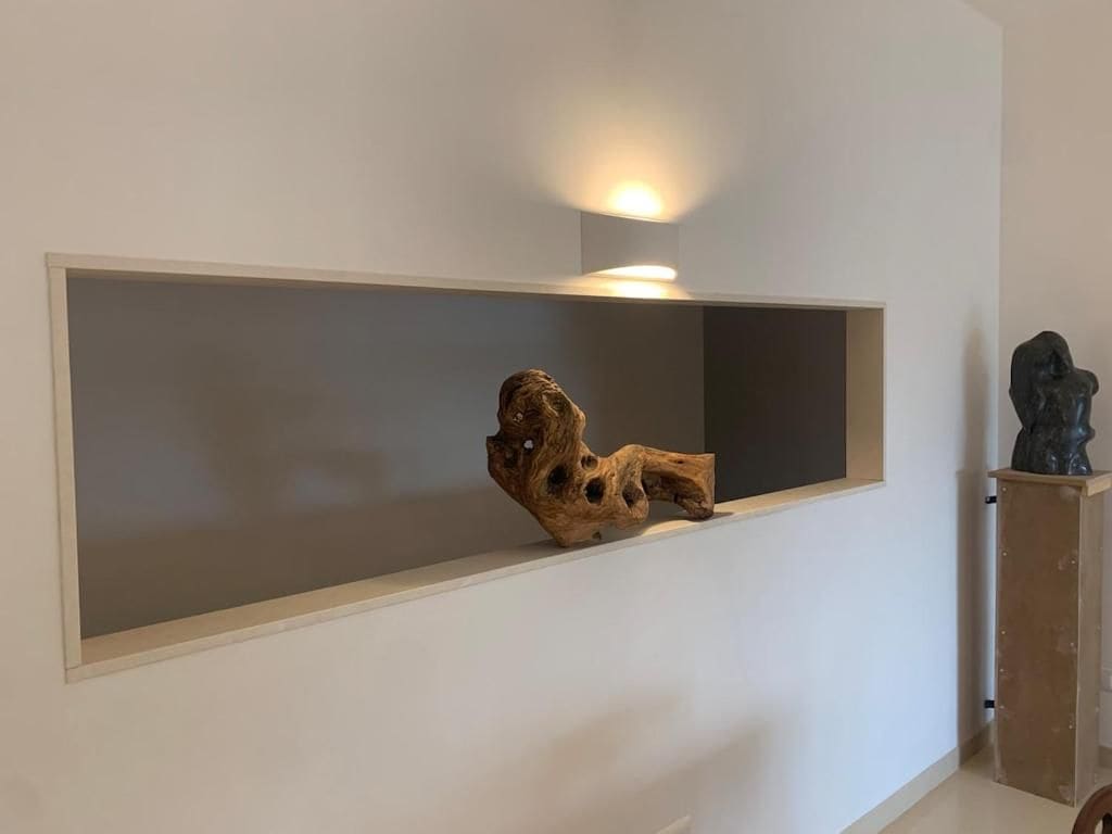 Uma prateleira na parede com uma escultura de madeira e uma pequena escultura em um pedestal.