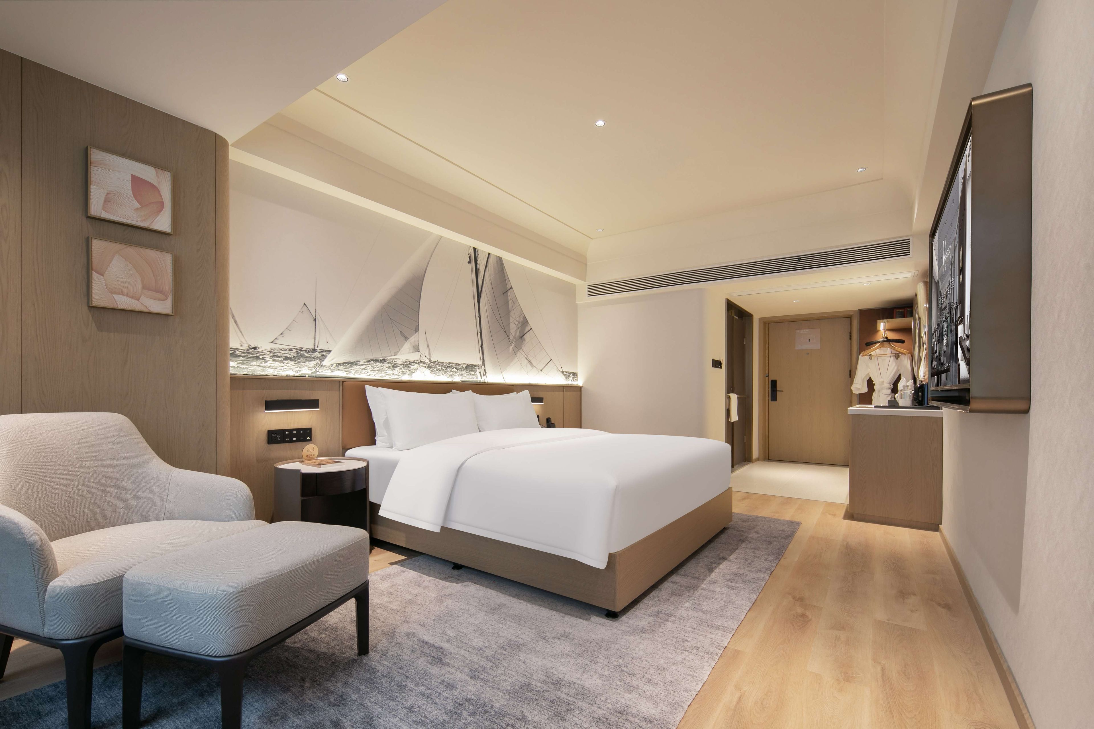 Quarto de hotel moderno com cama, área de estar, escrivaninha e uma grande obra de arte na parede.