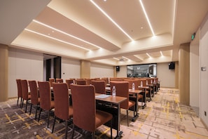 Sala de conferências com fileiras de cadeiras, mesas e uma tela de projeção.