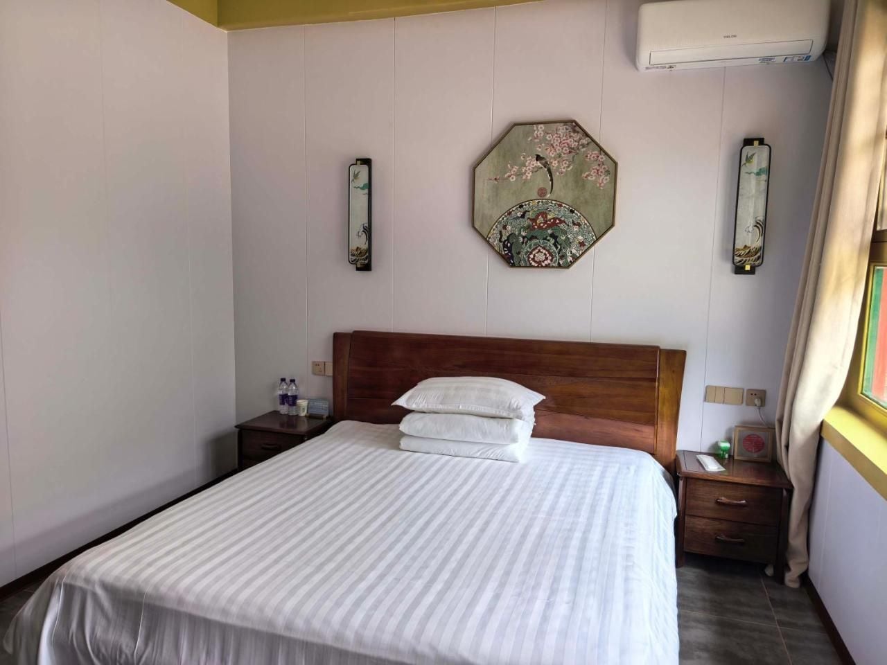 Uma cama bem arrumada com cabeceira de madeira, mesa de cabeceira com abajur e ar-condicionado fixado na parede.