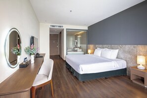 Quarto de hotel com cama, mesa de cabeceira, abajur, cadeira, escrivaninha e espelho.