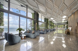 Um hall de hotel moderno com vista para o mar, áreas de estar e um balcão de recepção.