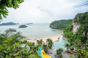 Um resort tropical à beira-mar, com vista clara para o oceano, praia arenosa e vegetação exuberante.