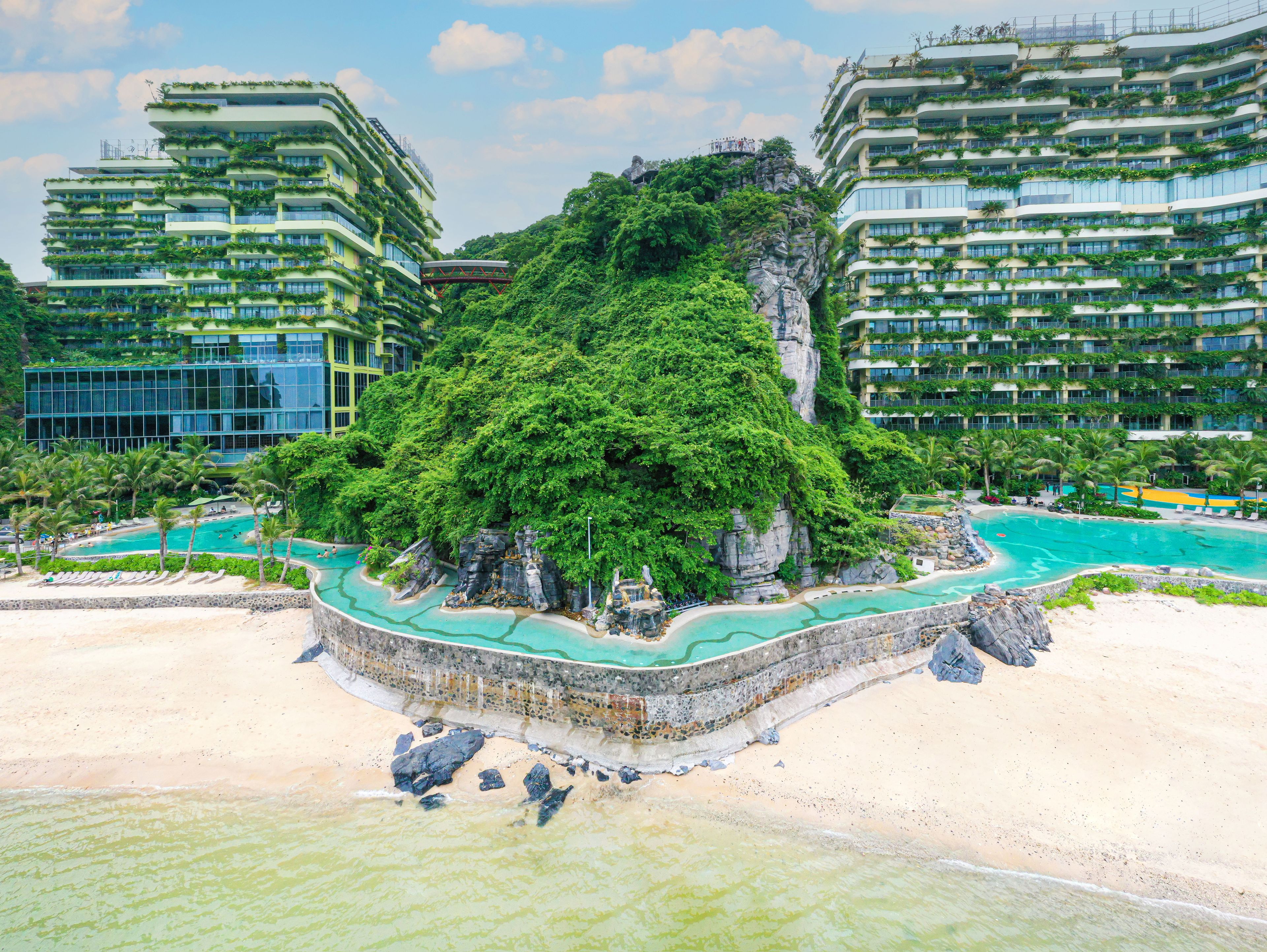 Resort com vários edifícios altos, uma formação rochosa central e área de piscina.