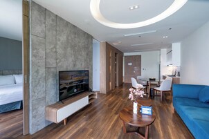 Quarto de hotel moderno com TV de tela plana, sofá, área de jantar e cozinha.