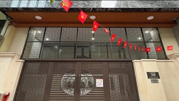 Fachada de prédio com um portão grande e decorativo, uma varanda com guarda-corpo e várias bandeiras vermelhas.