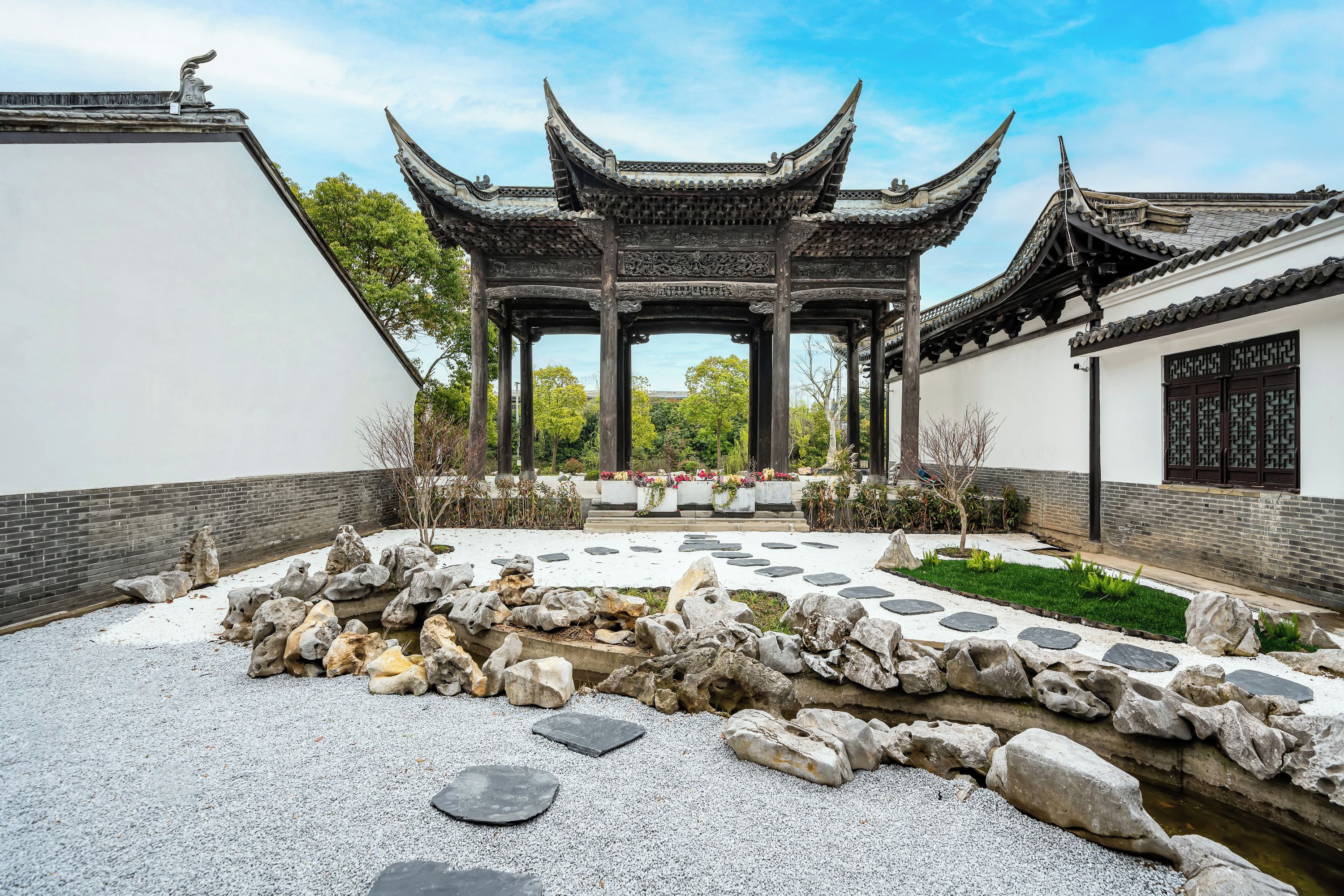Um pátio tradicional chinês com um pavilhão de telhado, degraus de pedra e um pequeno espelho d'água.