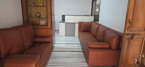 Uma sala de estar com dois sofás marrons, um aparador de madeira com objetos decorativos e uma mesa de console branca.