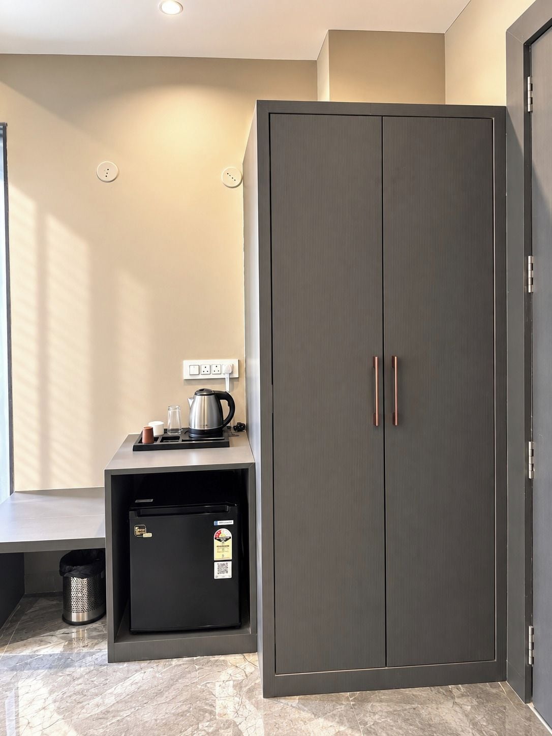 Quarto moderno com guarda-roupa espaçoso, pequena cozinha equipada com cafeteira e lixeira.