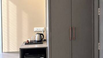 Quarto moderno com guarda-roupa espaçoso, pequena cozinha equipada com cafeteira e lixeira.