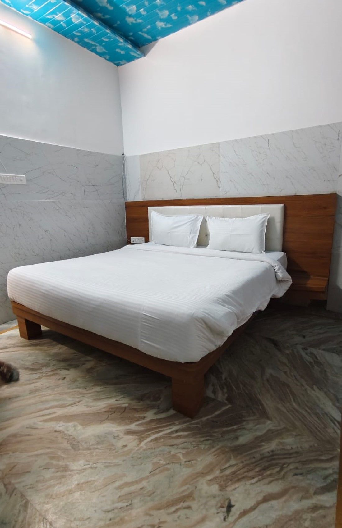 Quarto com cama, cabeceira de madeira, parede de mármore e teto azul.